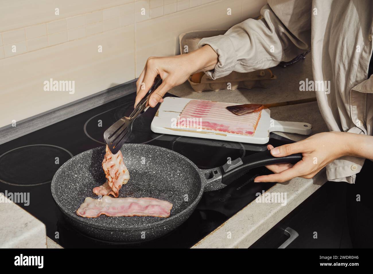 Hand of woman flipping bacon on frying pan with kitchen tongs Stock ...