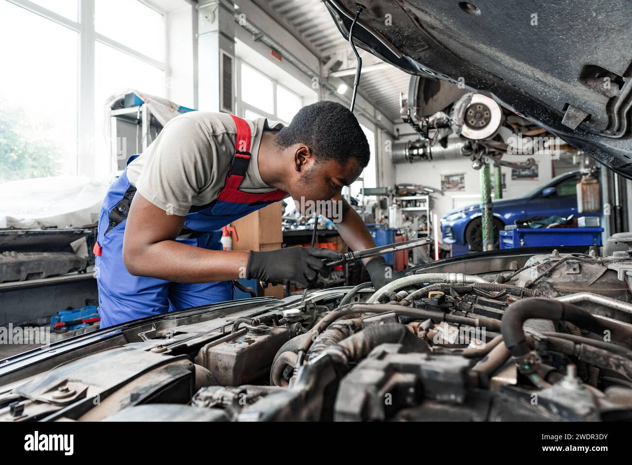 Young African auto mechanic checking car engine under the hood in auto ...