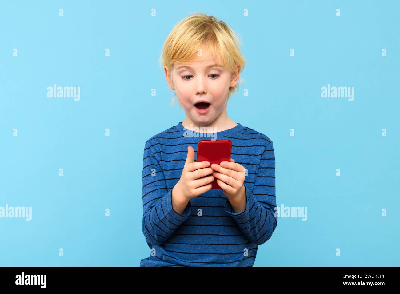 Young child holding smartphone, shocked with mouth open in disbelief ...
