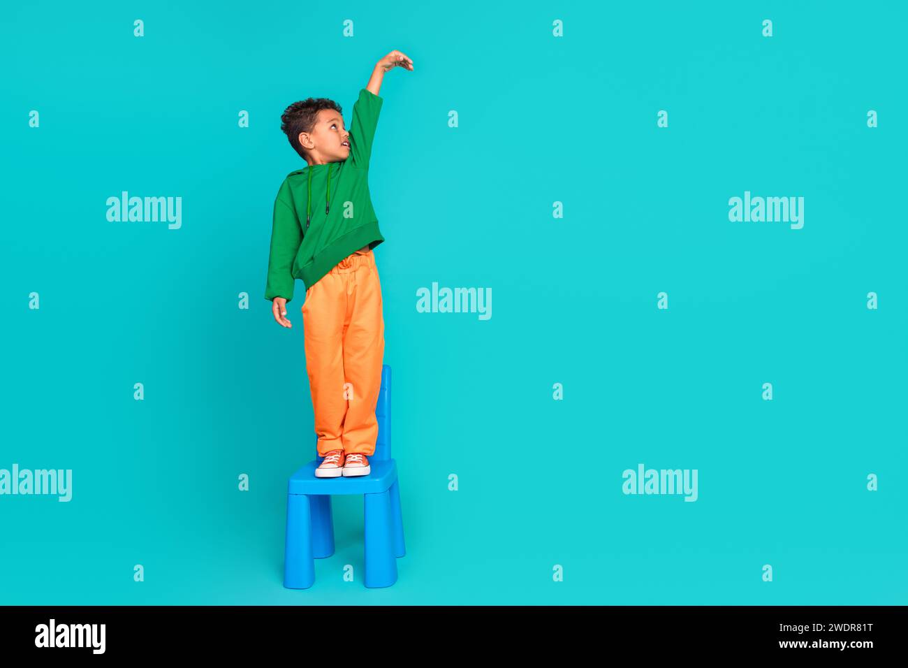 Full length photo of adorable preteen age boy standing on chair raise ...