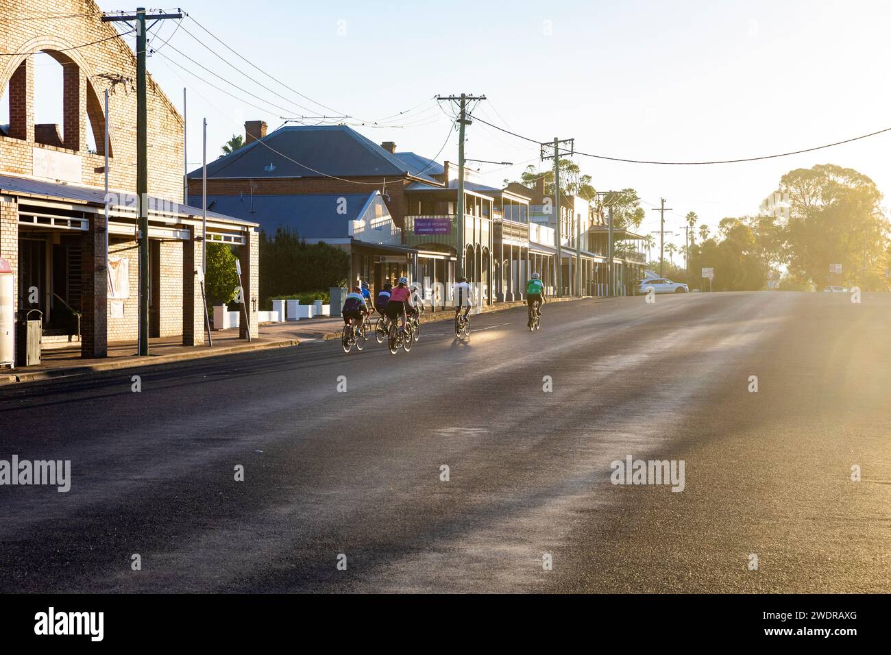 Road cyclists riding through Mudgee town centre, hazy sunny sunrise ...