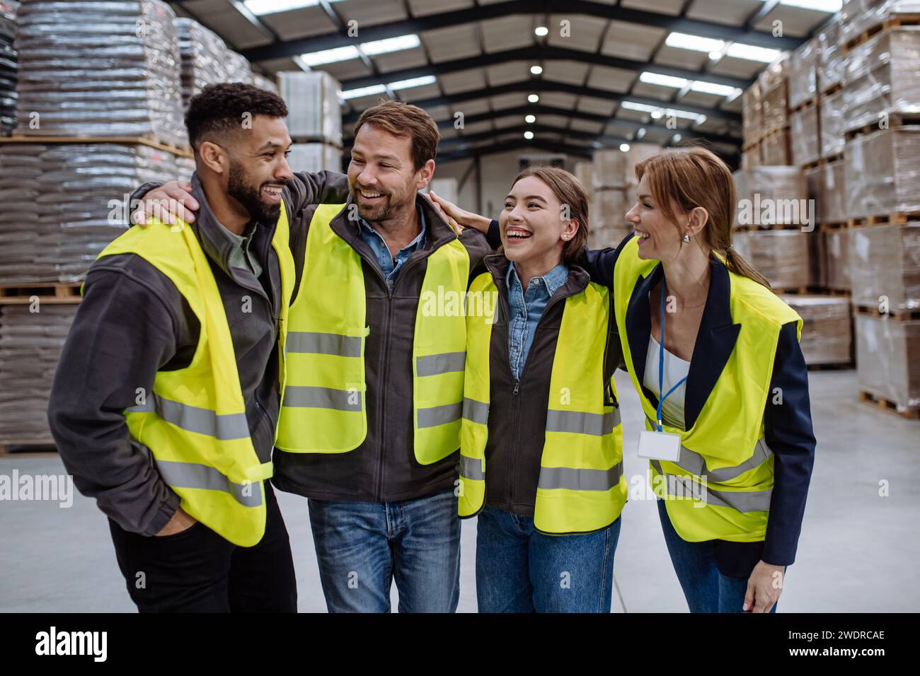 Full team of warehouse employees laughing in warehouse, holding each ...