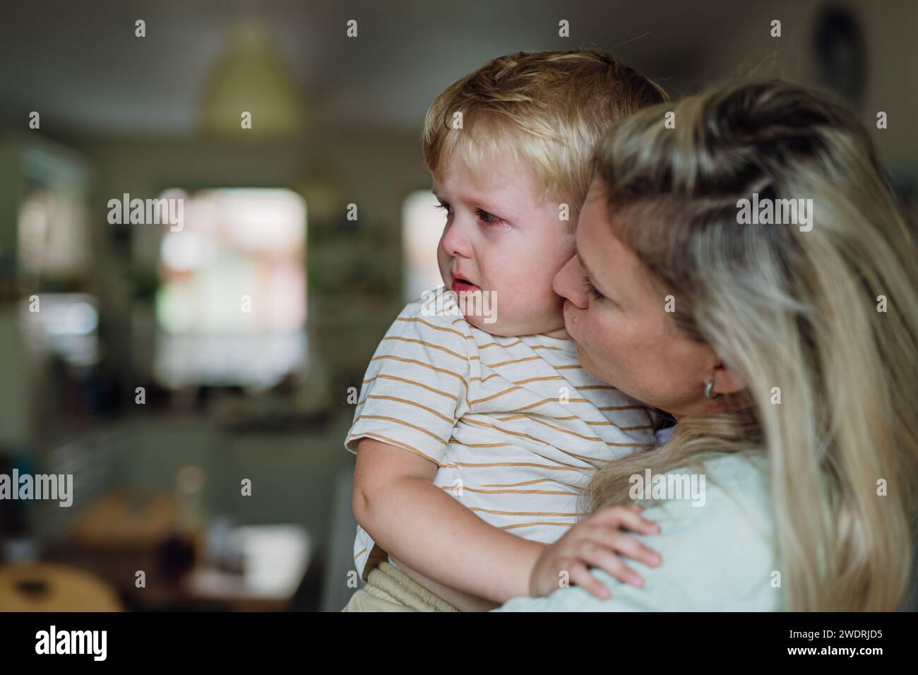Mother calming little son, holding him, kissing on cheek. Boy is sad ...