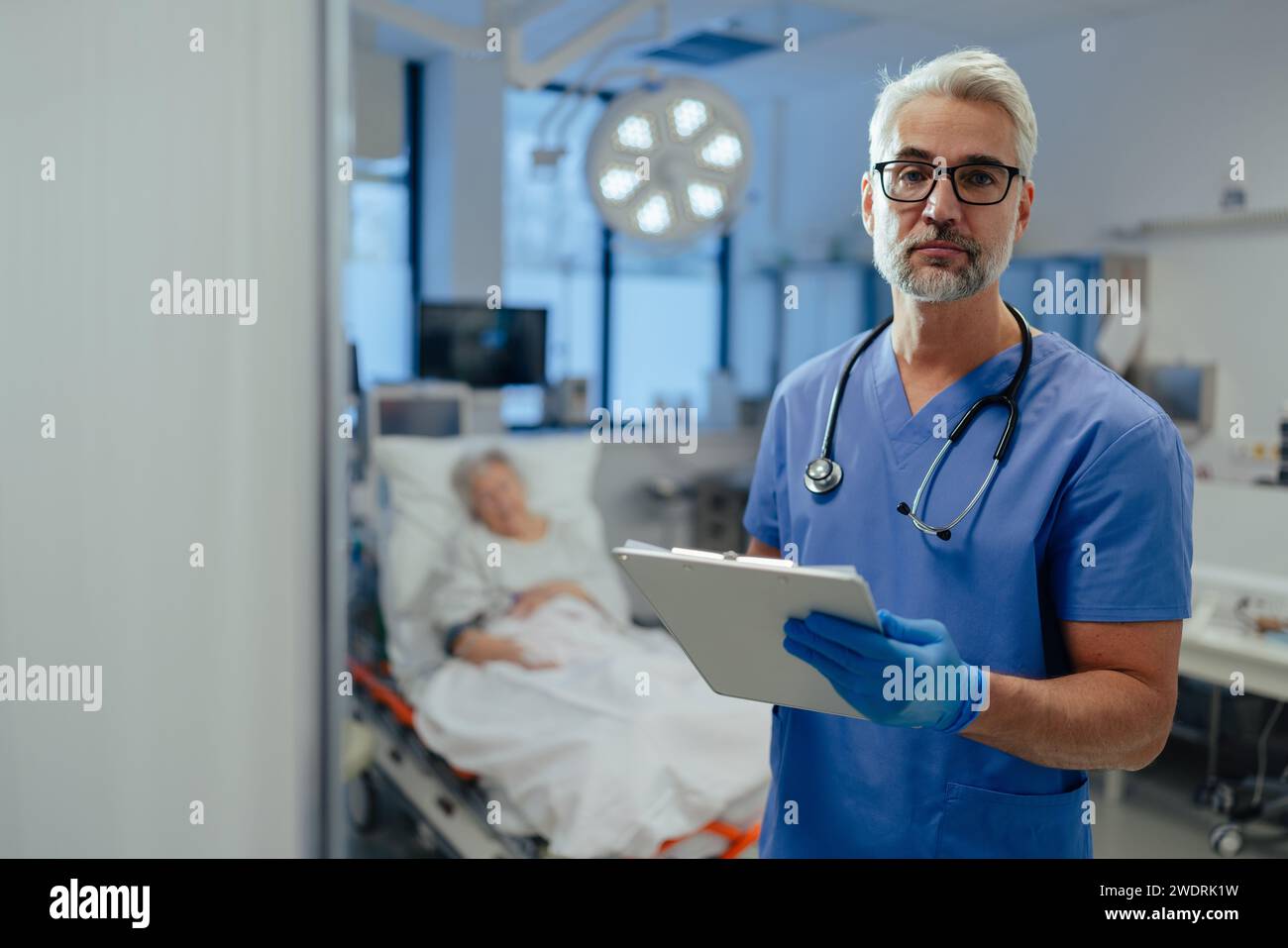 Portrait of handsome male doctor, patient in hospital bed behind. ER ...