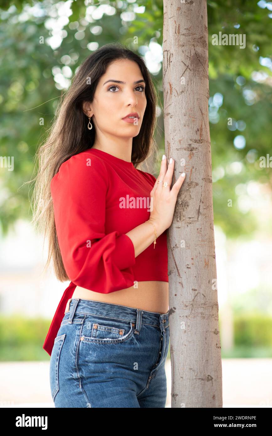 Beautiful woman leaning against tree looking away Stock Photo - Alamy