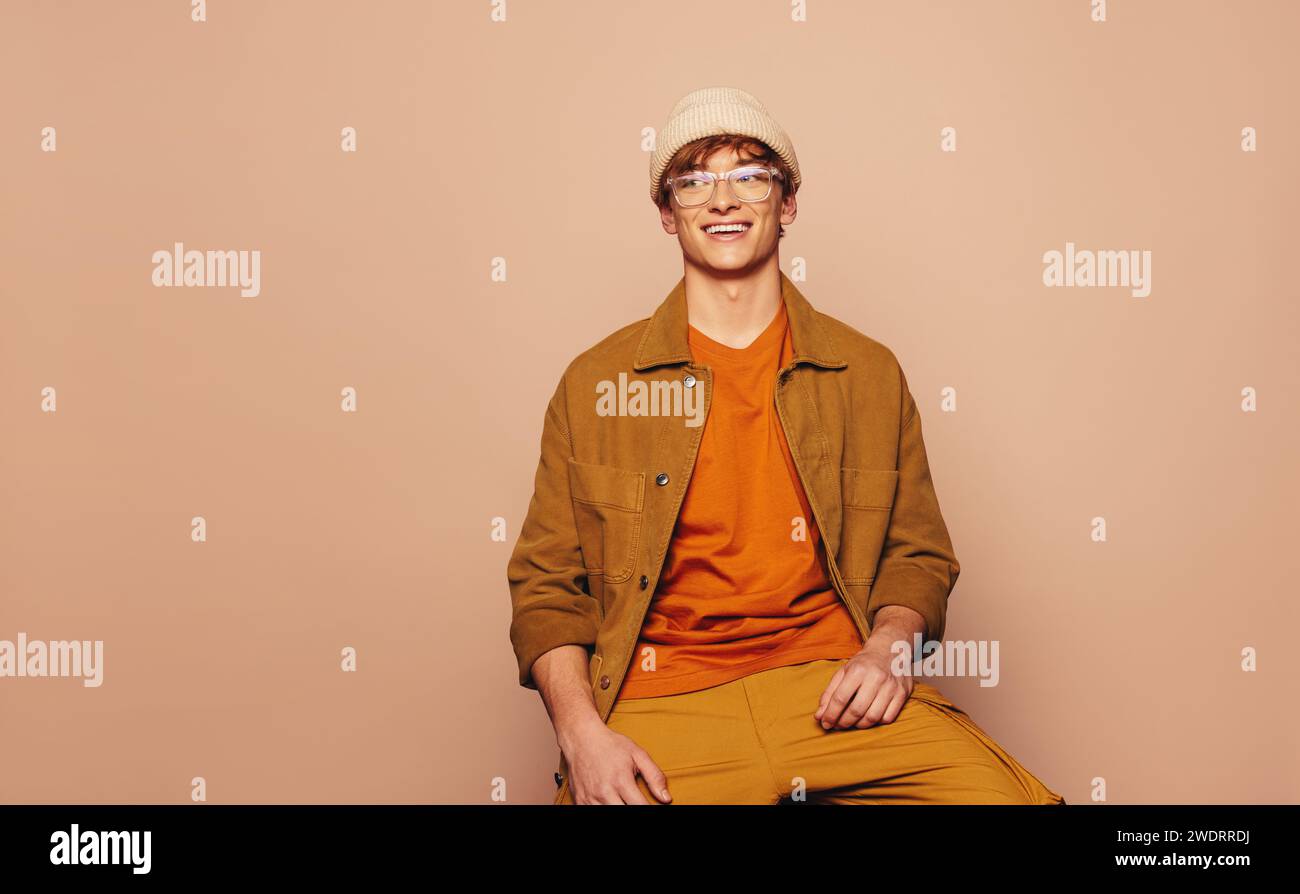 Stylish man in denim jacket, beanie, and glasses sits cheerfully on ...