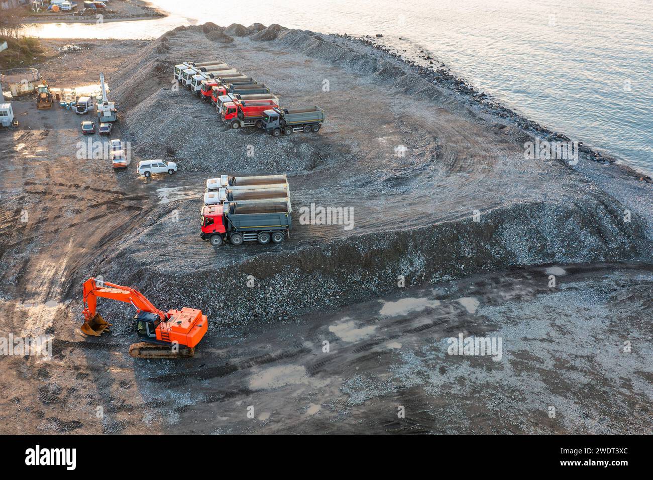 Aerial view of excavator and dump trucks during earthworks on construction site by the sea side ...