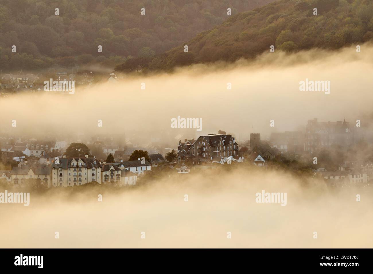 Sea fog envelops the coastal town of Lynton, lit by the light of sunset ...