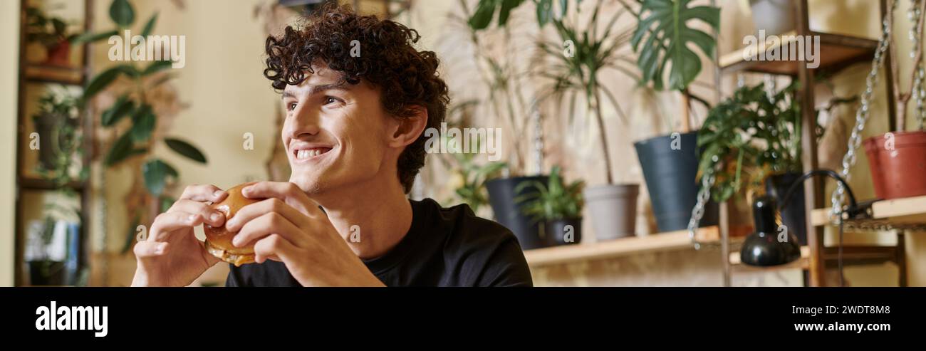 happy young man holding tofu burger and looking away while smiling in ...