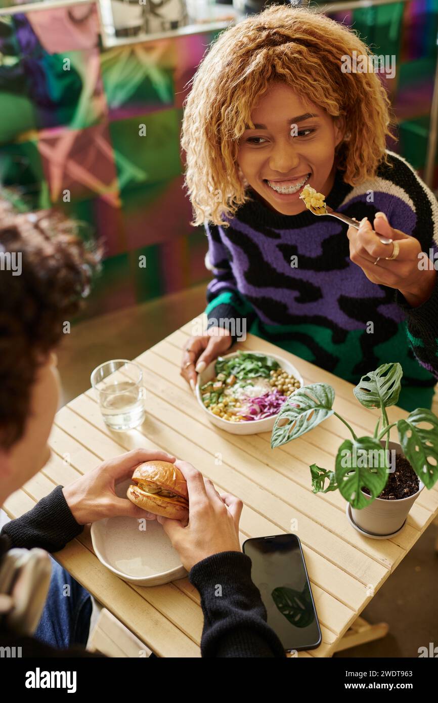 happy african american woman in braces eating delicious salad near man ...