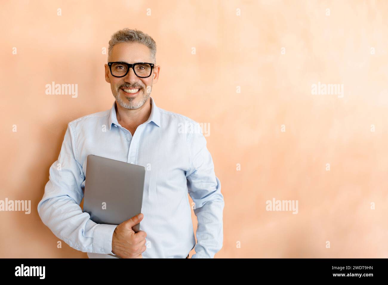 A relaxed yet confident mature businessman casually holds his laptop ...