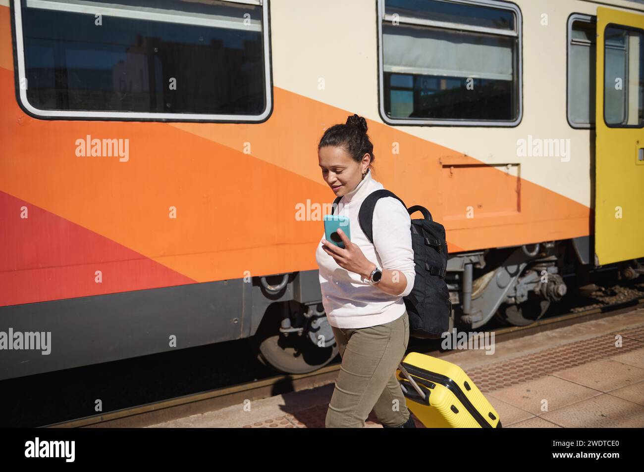 Smiling woman commuter harrying up to board train, carrying a suitcase ...
