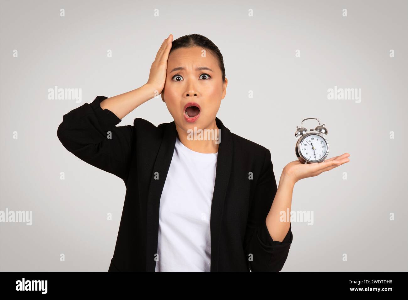 Shocked Asian businesswoman holding an alarm clock with a horrified expression Stock Photo - Alamy