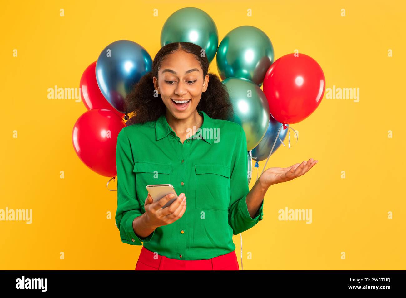 Excited African teenager girl texting on phone with balloons, studio ...
