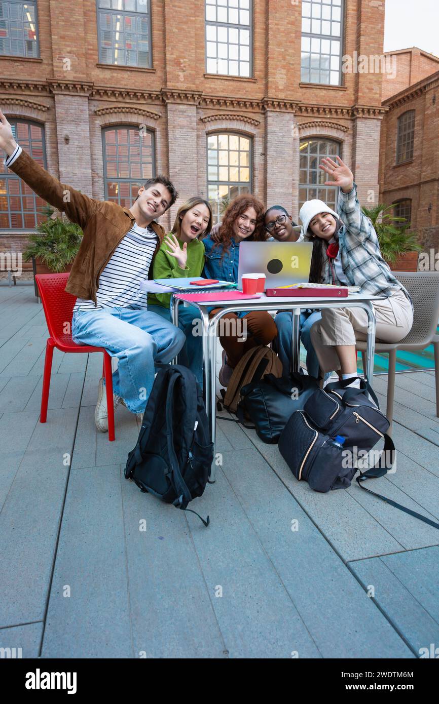 Group of smiling multiracial students with laptop sitting near campus preparing for the exam ...