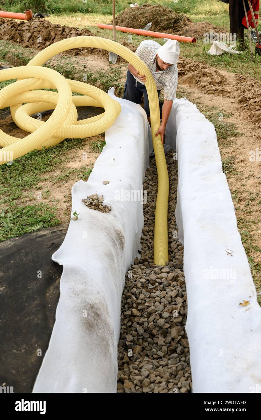 Groundwater drainage works in the field. A worker carries a yellow ...