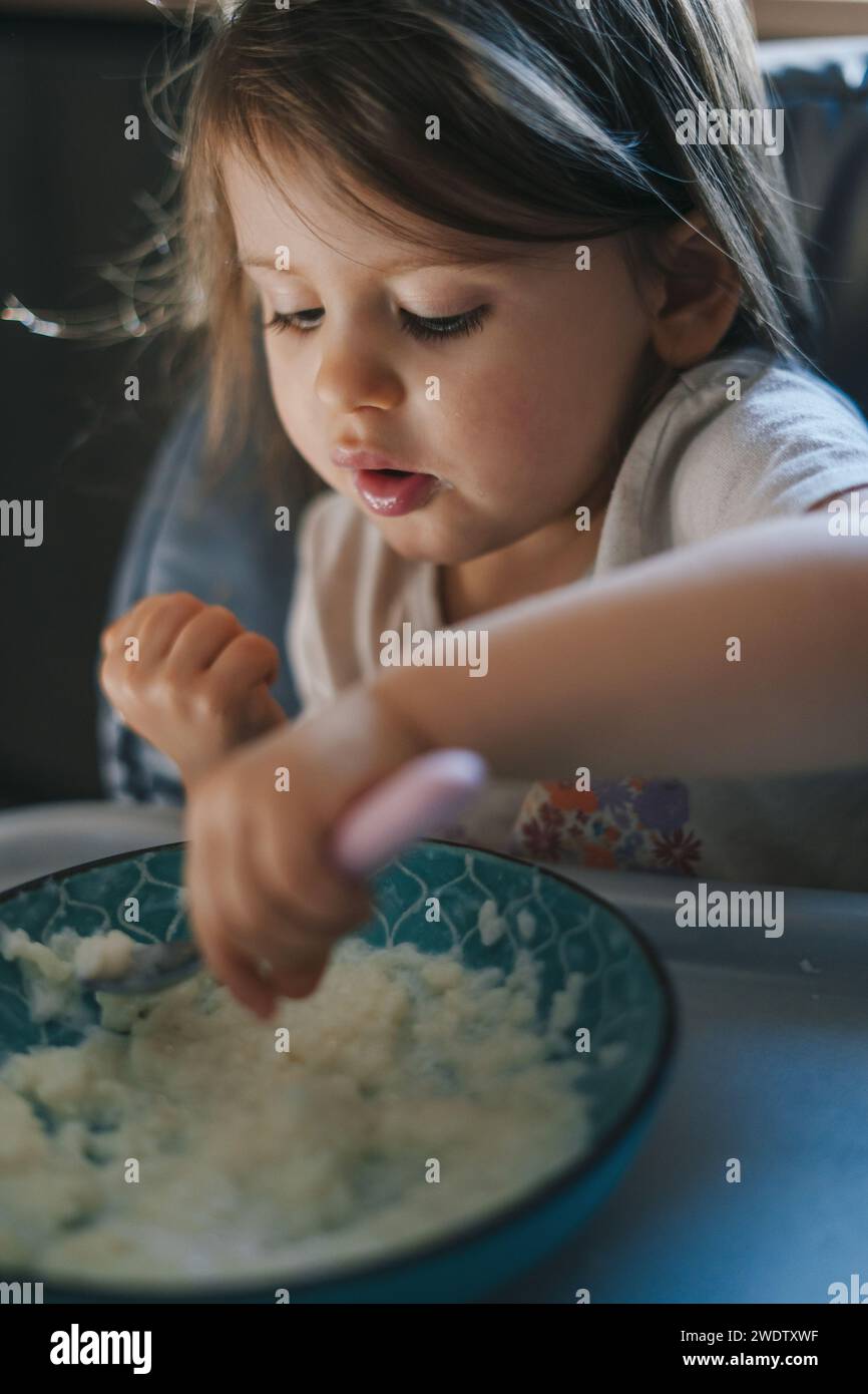 Cute kid girl enjoy eating rice on table for breakfast, holding spoon ...