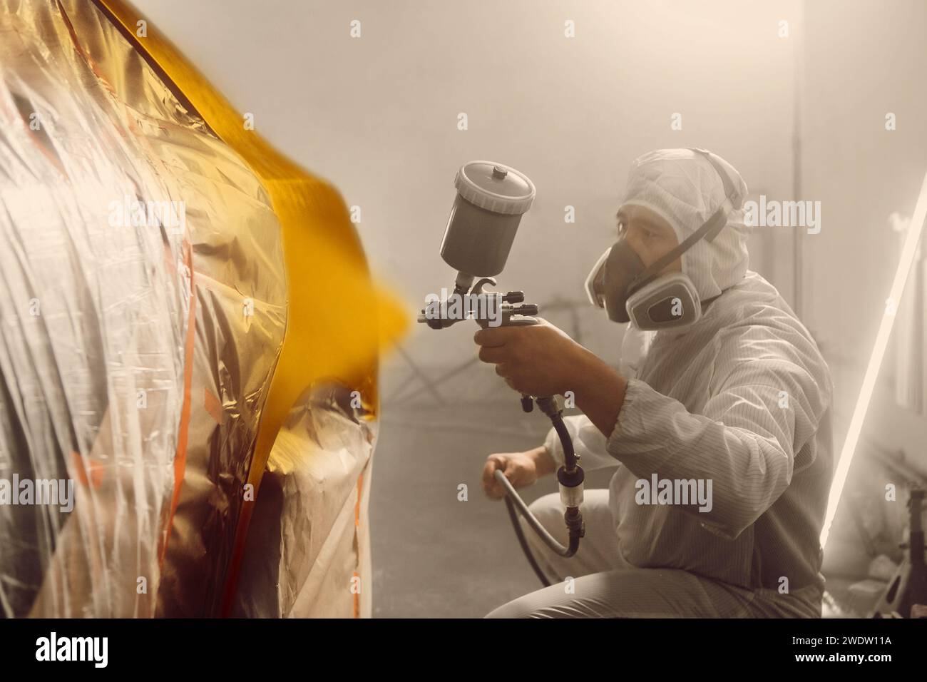 Auto mechanic worker spraying car body to orange gold color using spray ...