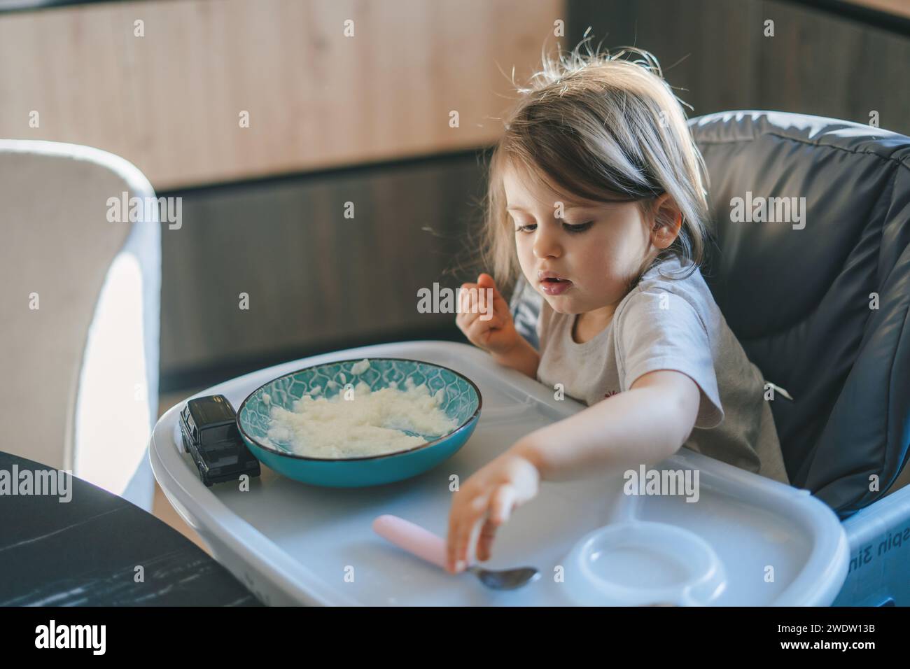 Portrait of a little girl sitting on the chair and eating fried rice by ...