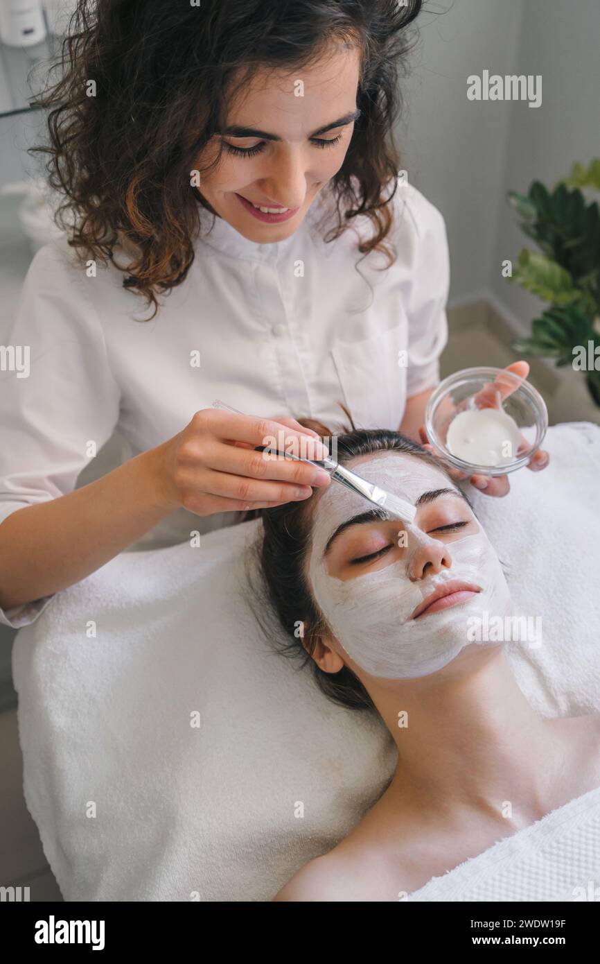 Beautiful woman having clay facial mask apply by beautician. Relaxing ...