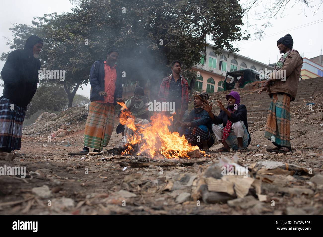 Dhaka, Bangladesh. 22nd Jan, 2024. Workers warm themselves around a bon ...