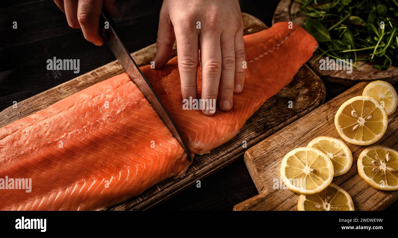 Chief hands cut salmon fillet with knife on wooden table at kitchen ...