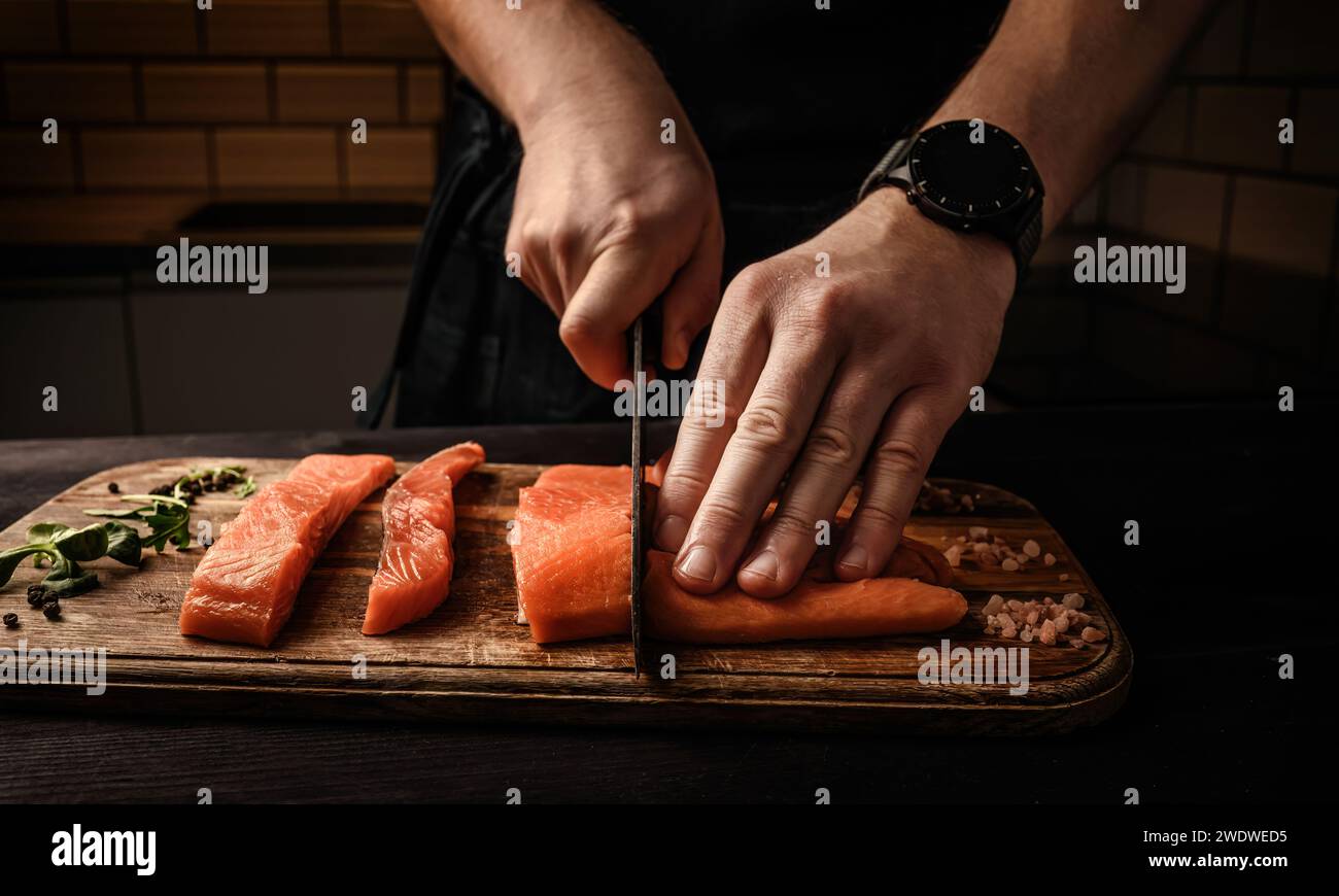 Mle cutting red Salmon fish on a cutting board with a big kitchen knife ...