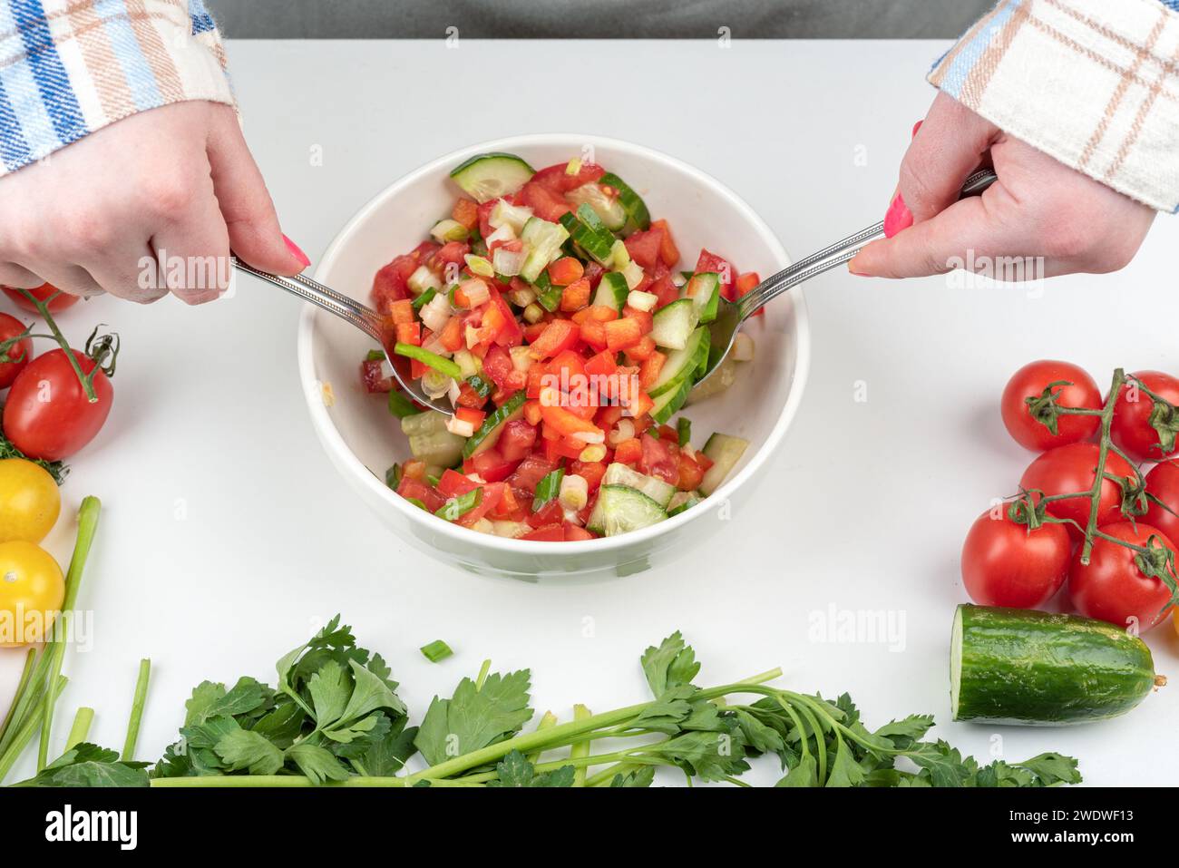 Vegetable salad seasoned with oil is mixed with spoons. Women's hands ...