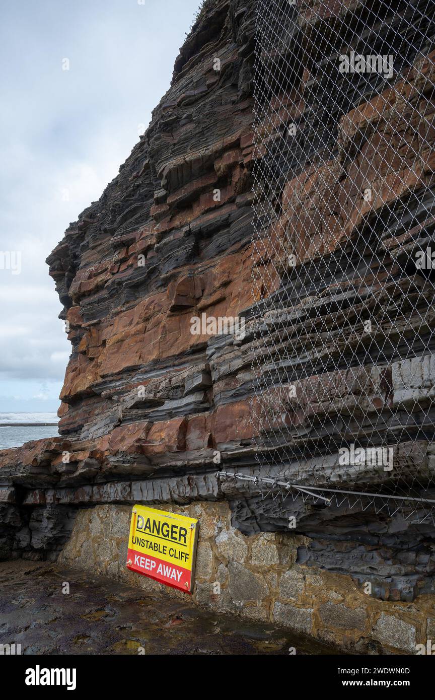 a warning sign in front of an unstable cliff which has had a wire ...