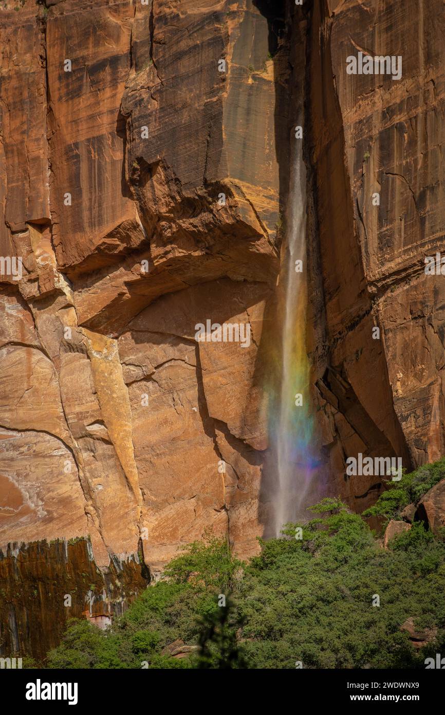 Small waterfall in front of a red rock face is illuminated by the sun ...