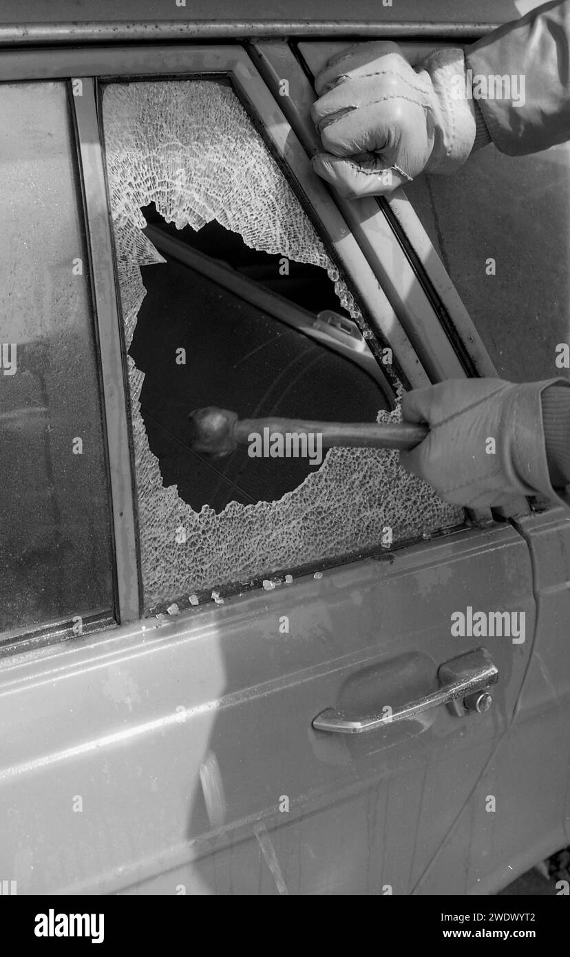 1970s, historical, a gloved hand car thief smashing a car window, a ...