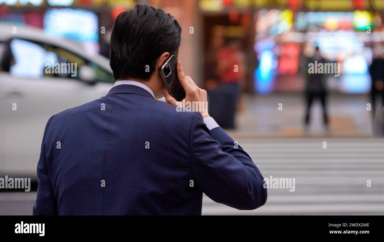A Japanese businessman stands patiently in the crosswalk, using a smartphone in hand to make a ...