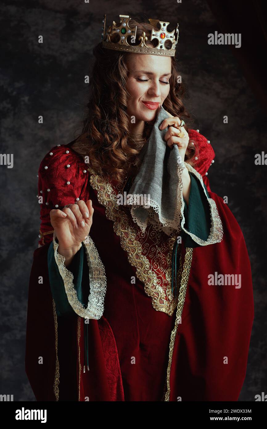 smiling medieval queen in red dress with handkerchief and crown on dark ...