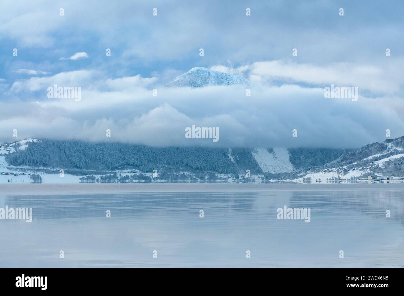 A tranquil winter landscape showcases a snow-capped mountain shrouded ...