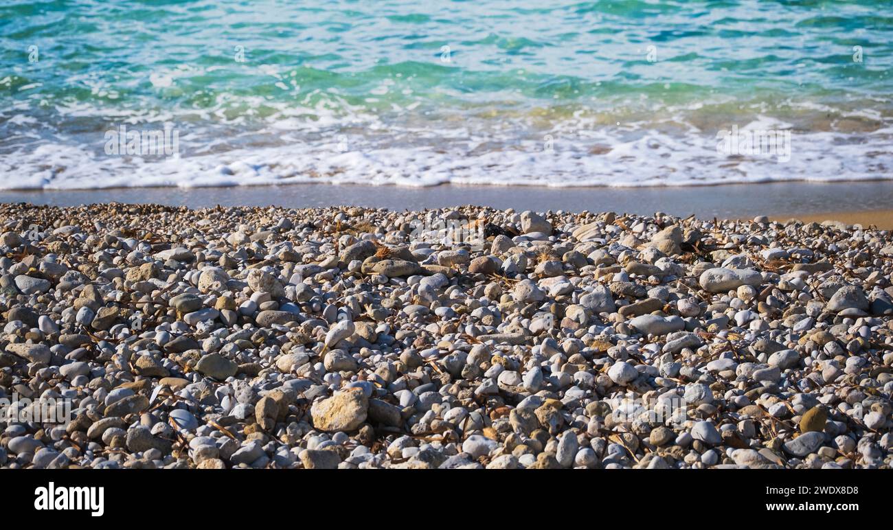 Pebble beach with turquoise water and waves. Stone beach on a sunny day ...