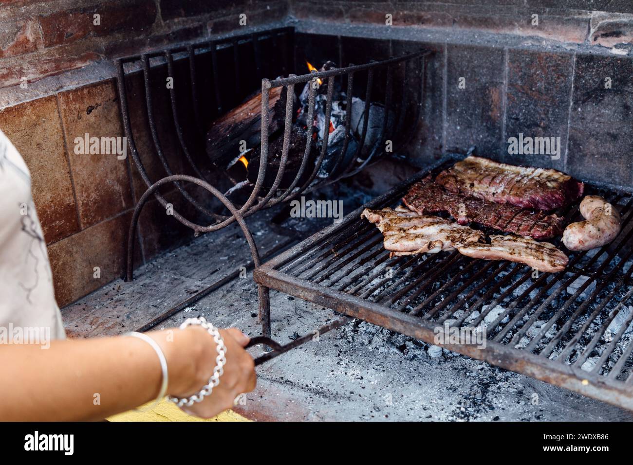 Woman making a barbecue. She is adding embers under the meat Stock ...