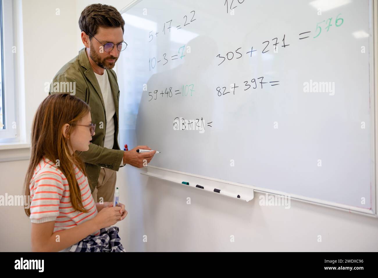 School teacher watching pupil writing on white board in classroom Stock ...