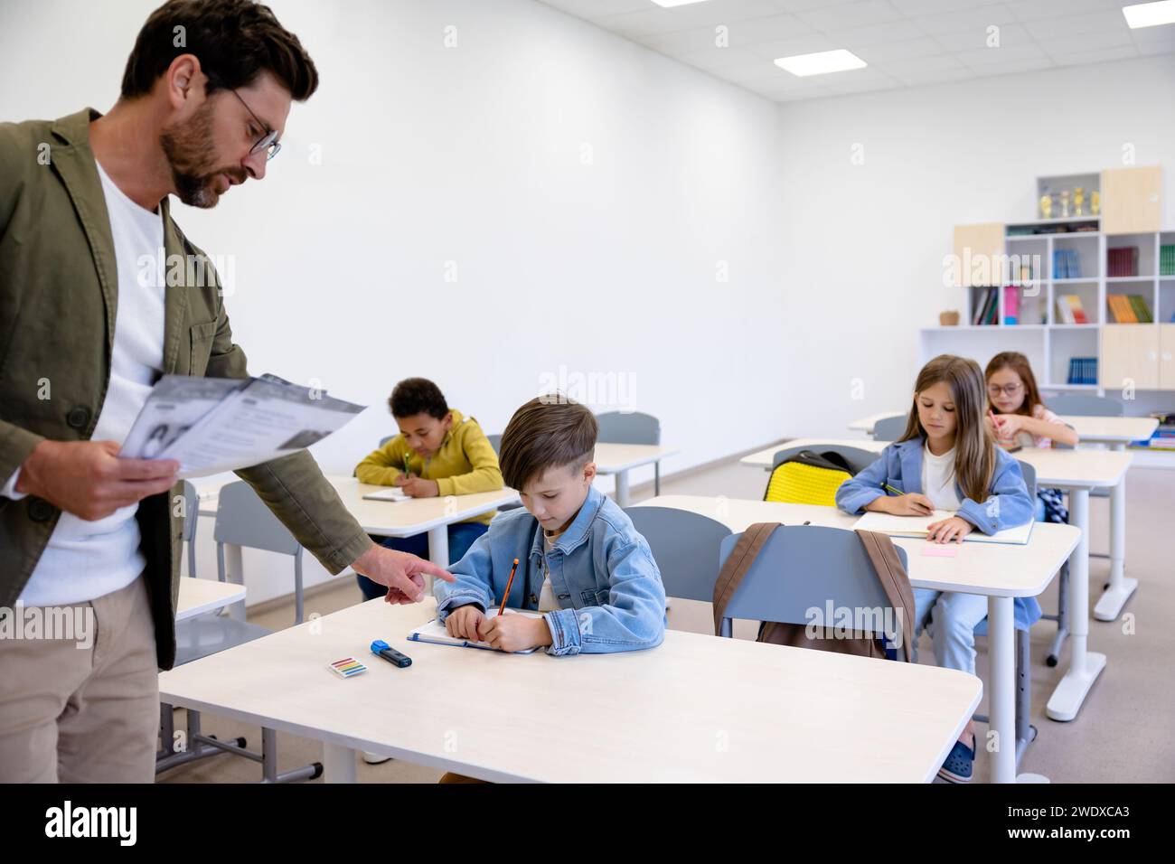Male giving tasks on paper to pupils in classroom Stock Photo - Alamy