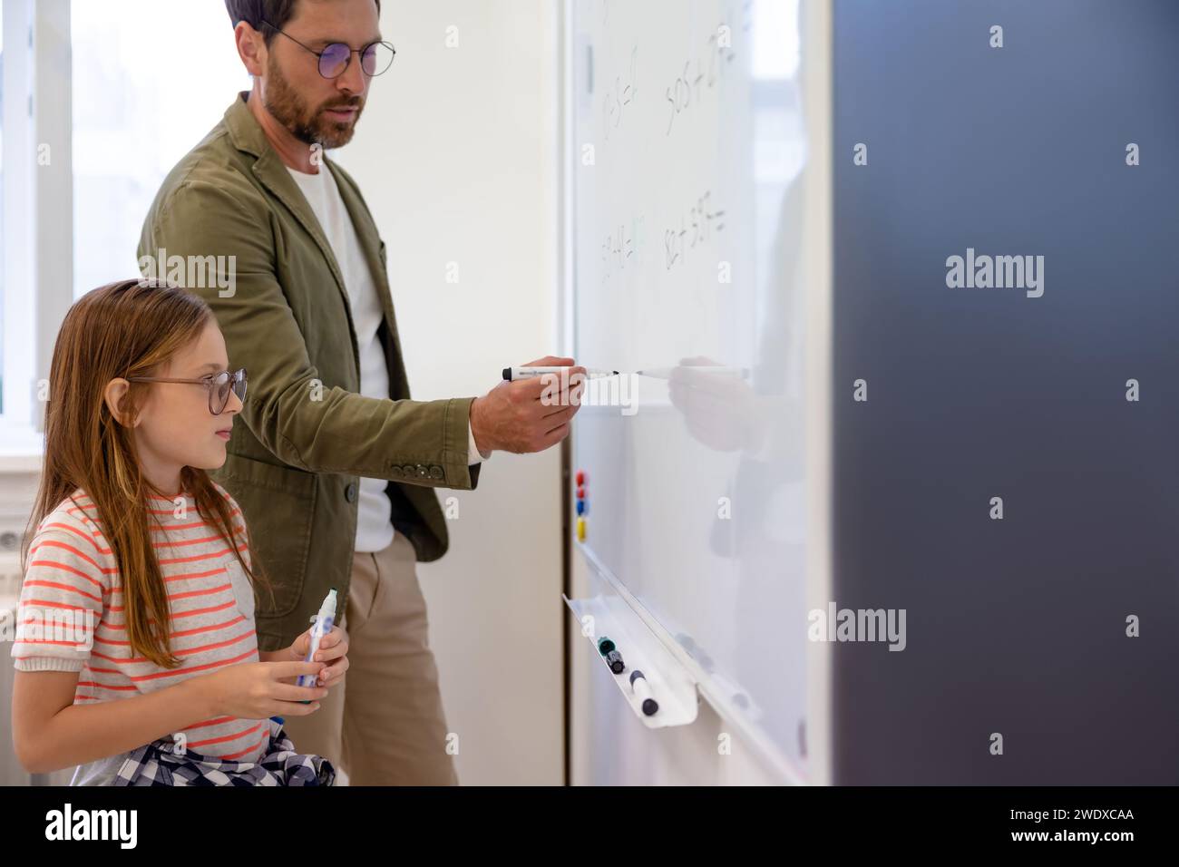 School teacher watching pupil writing on white board in classroom Stock ...