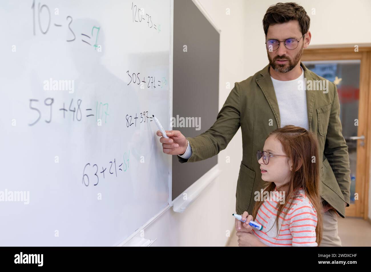 School teacher watching pupil writing on white board in classroom Stock ...