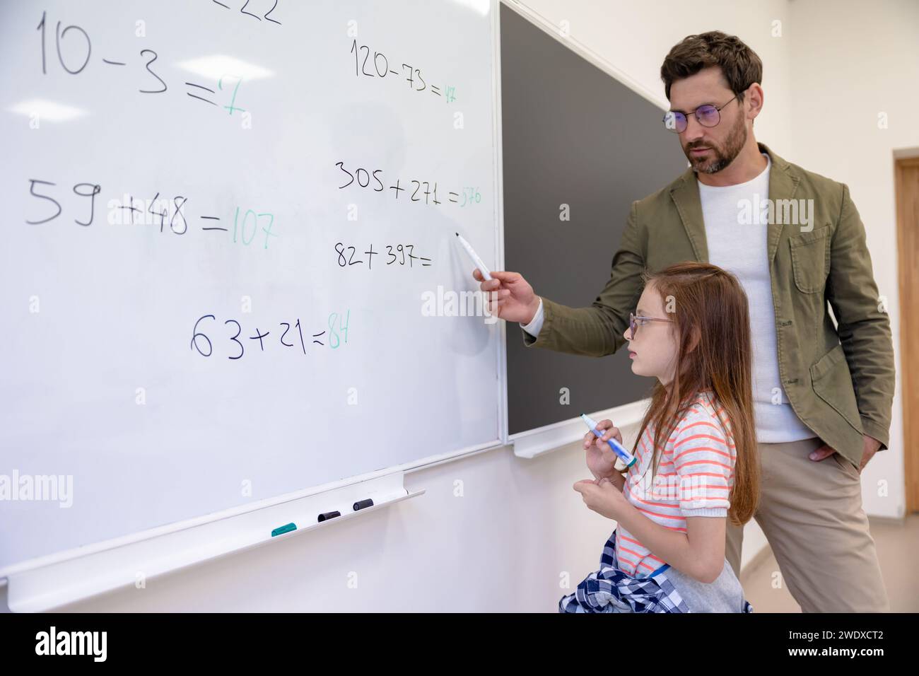 School teacher helping pupil writing on white board solving math ...