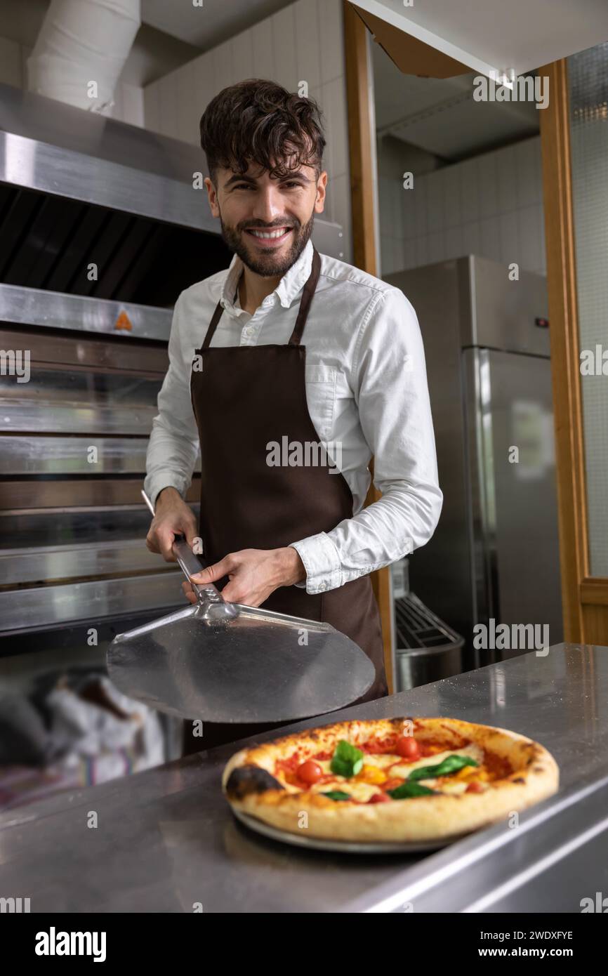 Dark-haired young man cooking pizza in pizzeria Stock Photo - Alamy