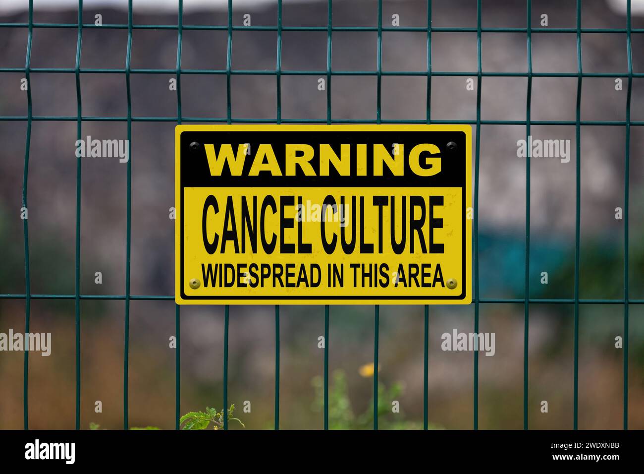 Yellow and black warning sign on a fence stating in "Warning - Cancel ...