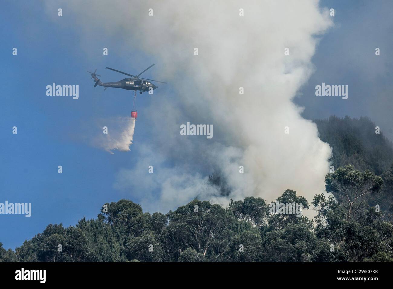 A helicopter sprays a wildfire fire in the mountains overlooking ...