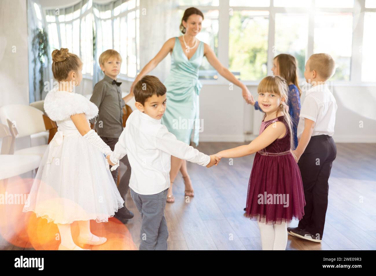 Little children in elegant dresses doing round dance in school hall ...