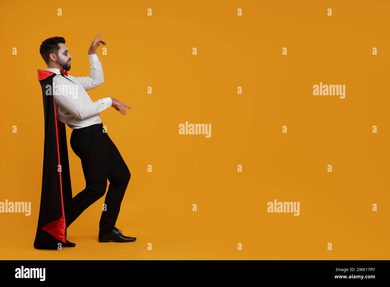 Man in scary vampire costume with fangs posing on orange background ...