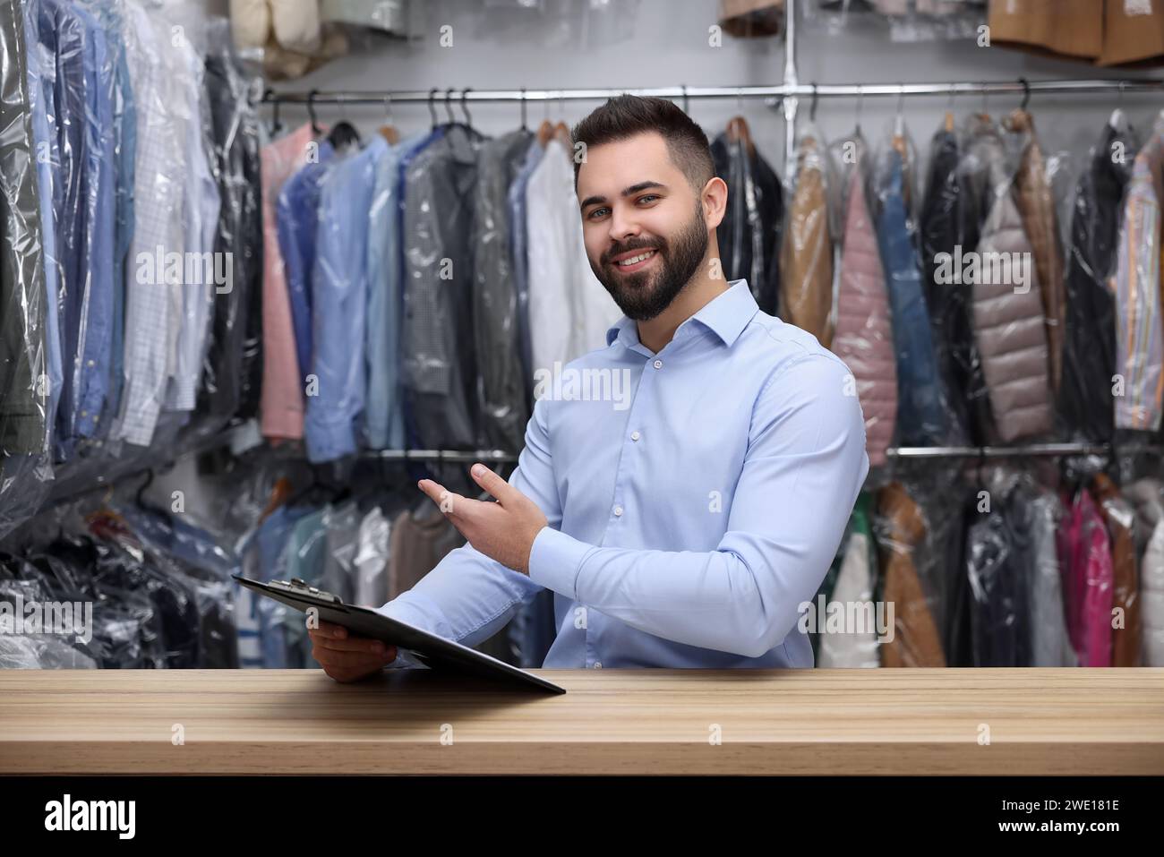 Dry-cleaning service. Happy worker holding clipboard at counter indoors ...