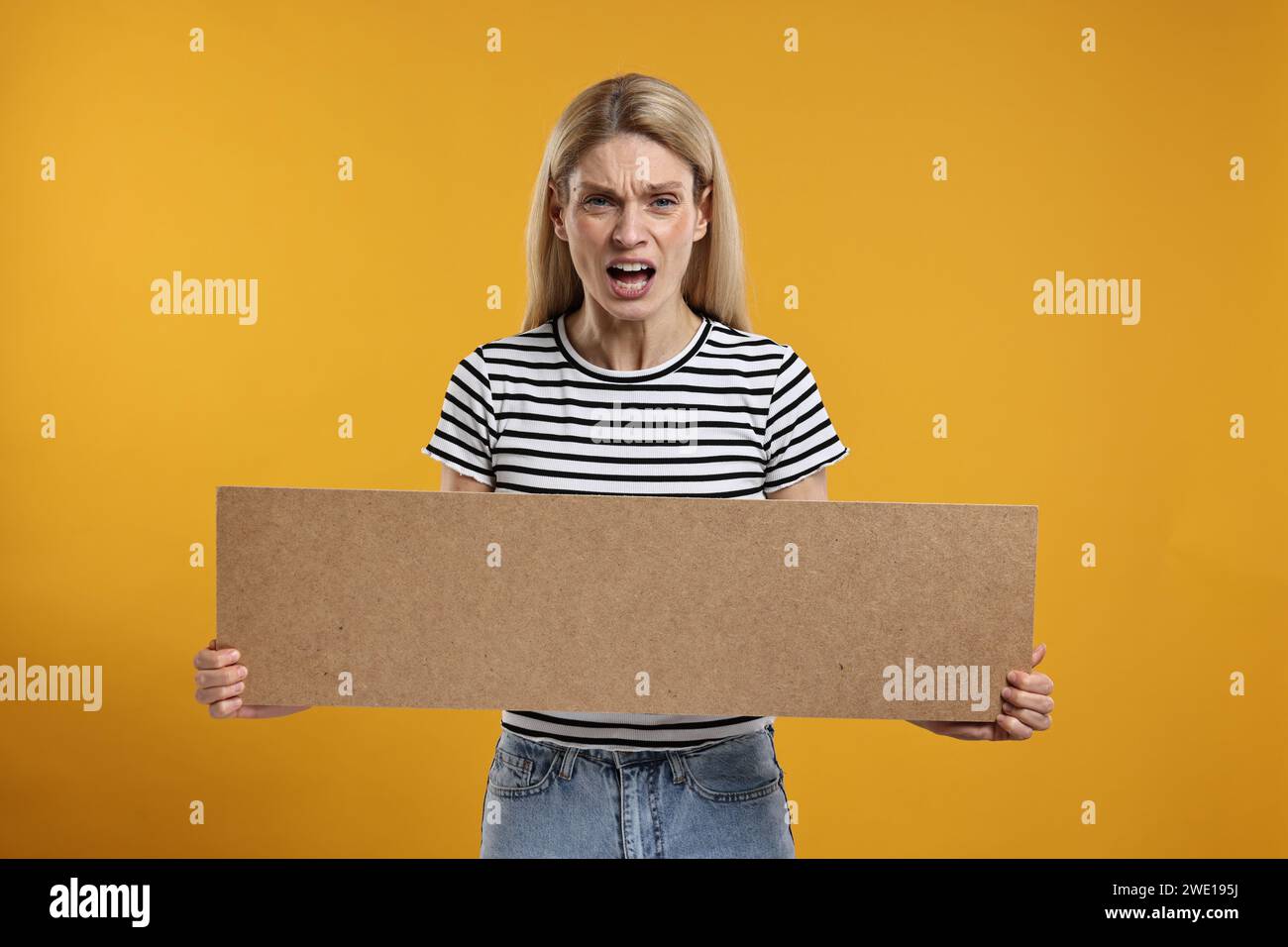 Angry woman holding blank cardboard banner on orange background, space ...