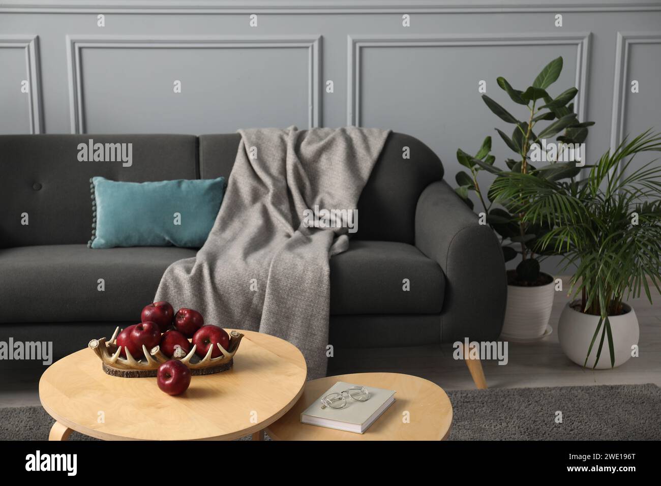 Red apples on nesting tables, sofa and houseplants in room Stock Photo ...