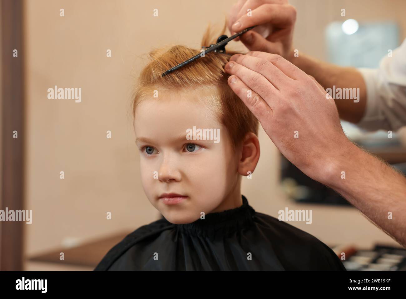 Professional hairdresser combing boy's hair in beauty salon, closeup ...